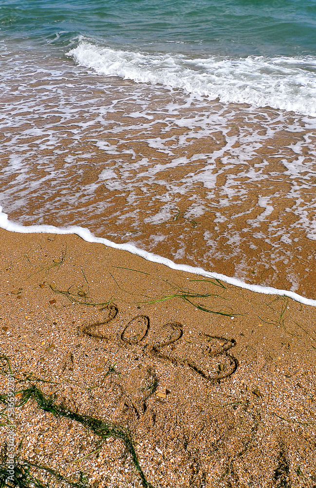 2023 written on the beach sand. Bright turquoise green sea waves with ...