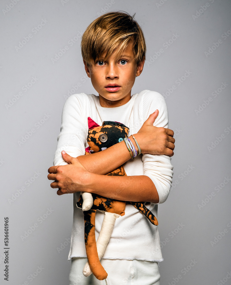 Scared child in pajamas standing and clutching his stuffed toy tightly ...