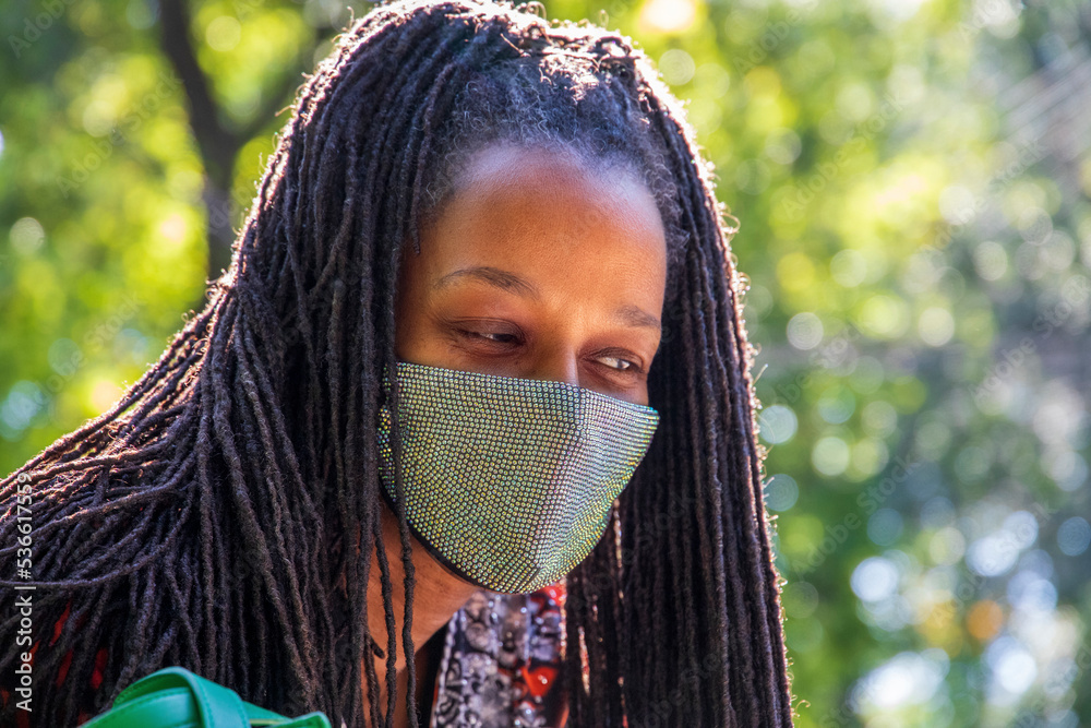 an African American woman with long braids wearing a mask and an orange ...