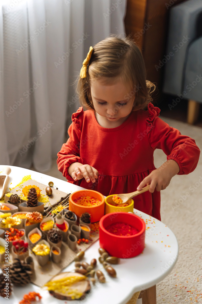 A little girl playing with autumn natural materials and make a tree ...