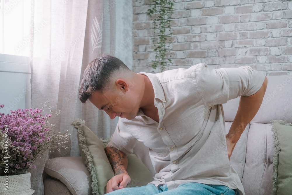 One young man suffering low back pain at home alone. Stressed injury ...