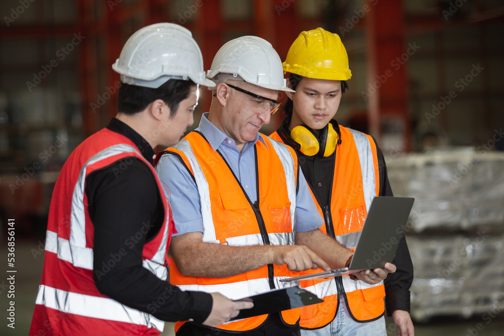Three man industrial engineers wear hard hats and uniform using laptop talking project of ...