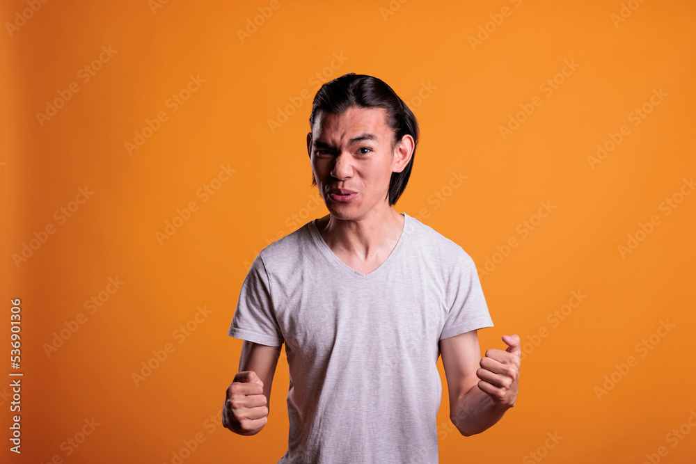 Foto de Angry young asian man clenching fists with furious facial ...
