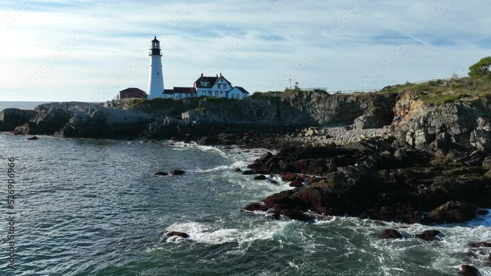 Rocks and ocean waves with lighthouse. Aerial pullback reveal of scenic ...
