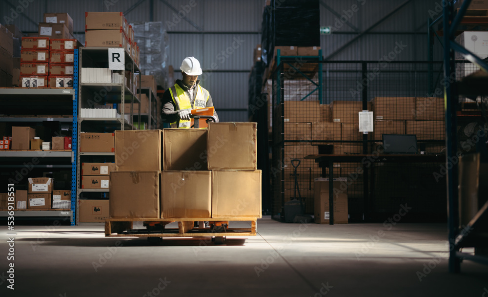 Logistics worker reading a clipboard while moving goods with a pallet ...