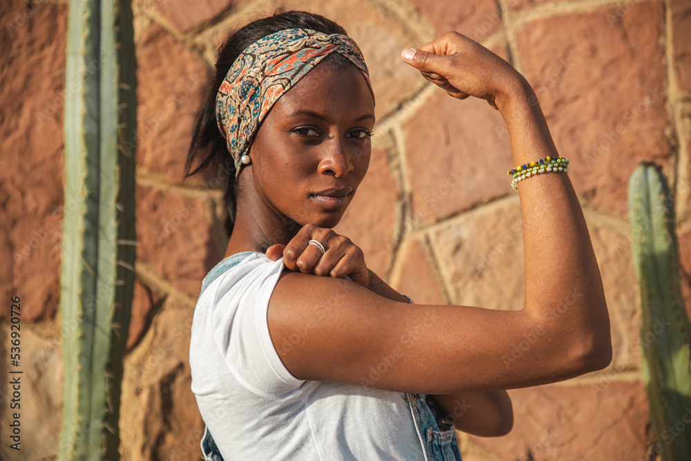 Confident woman flexing muscle in front of wall with cactus plant Stock ...