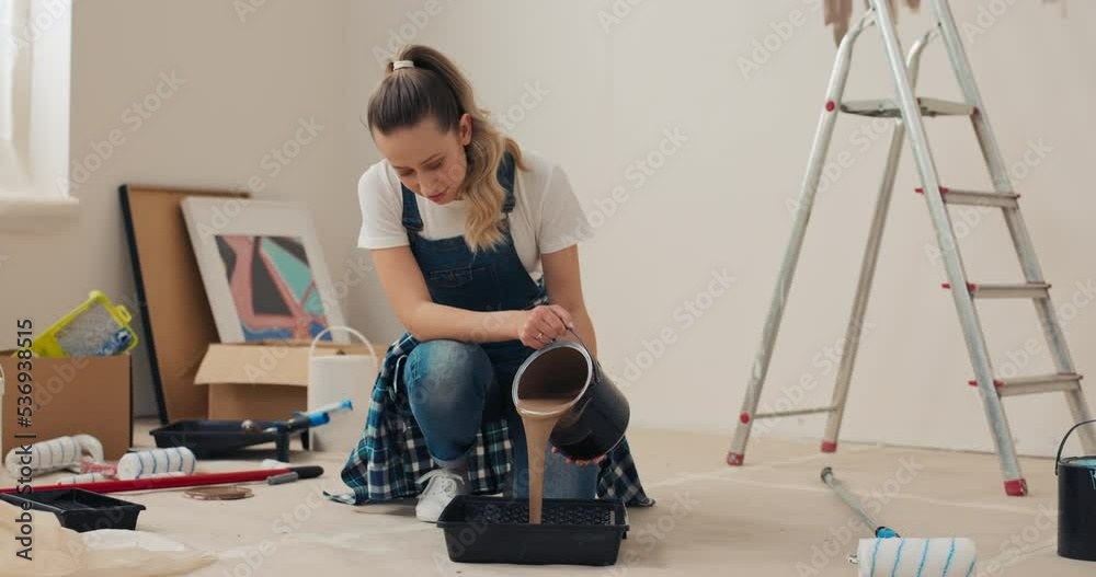 Woman with blond curly hair holds bucket of brown paint in hands and ...