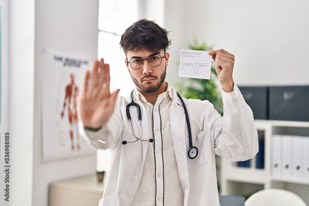 Hispanic doctor man with beard holding covid record card with open hand ...