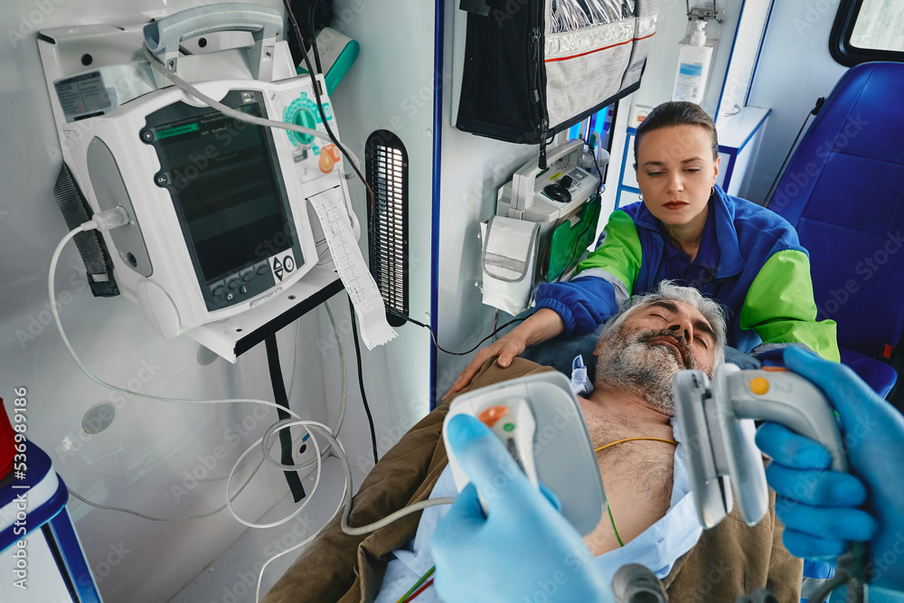 First aid in ambulance. Paramedic with defibrillator pads before CPR ...