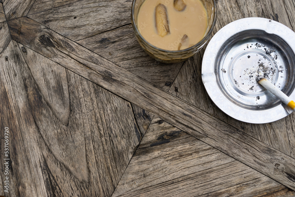 Wooden table with ashtray filled with cigarettes ashes and ice coffee ...