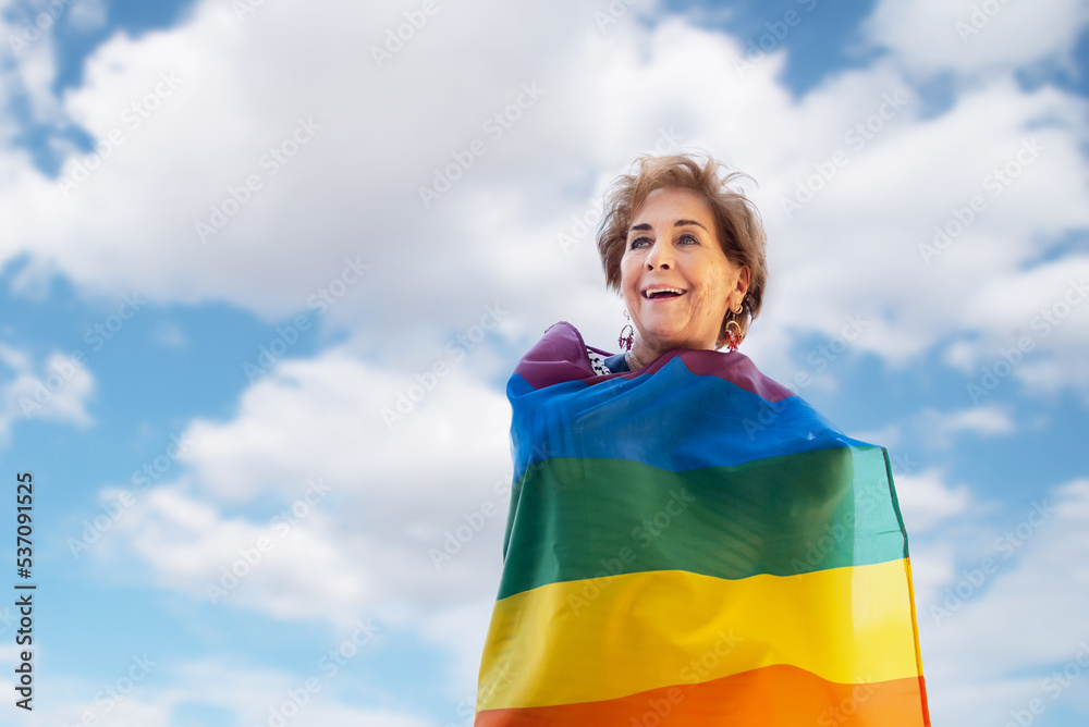 Older lady smiling, surrounded by the rainbow colored flag representing ...