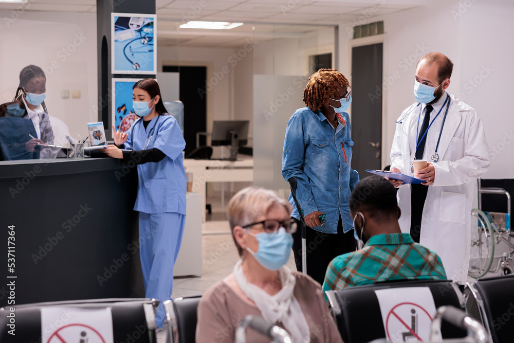 Asian female physician, african american receptionist checking patient ...