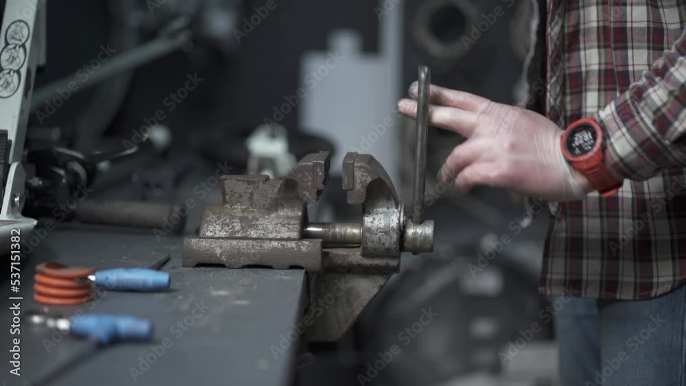 A male mechanic uses a metal vise to repair a scooter in the ...