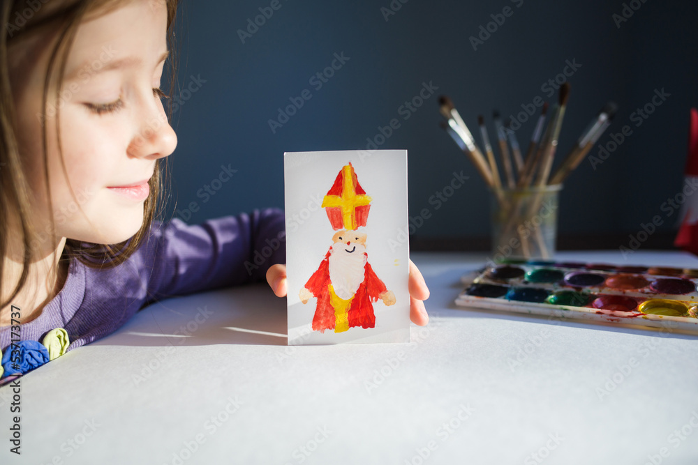 girl shows children's drawing - card for day of saint nicholas on table ...