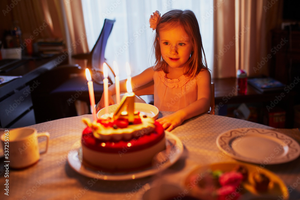 Happy little girl celebrating her fourth birthday and making a wish ...