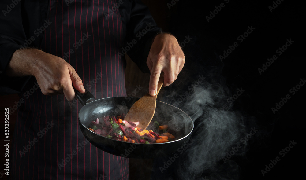 Professional chef prepares food in a frying pan with steam on a black ...