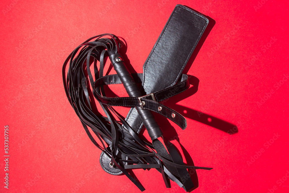 BDSM accessories on a red background. A leather paddle, padded ...