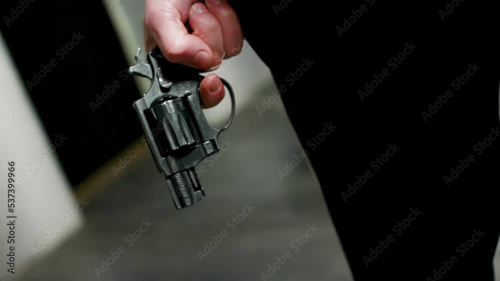 Close-up guy lowers his hand with revolver pistol to his leg in black ...