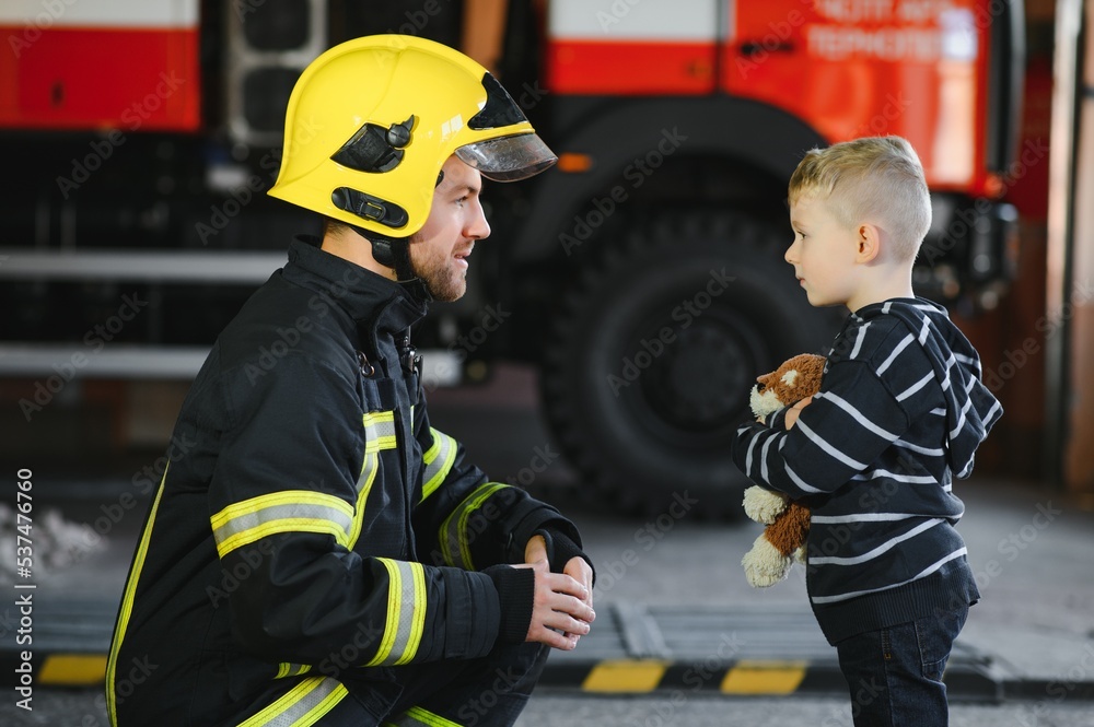 Portrait of rescued little boy with firefighter man standing near fire ...