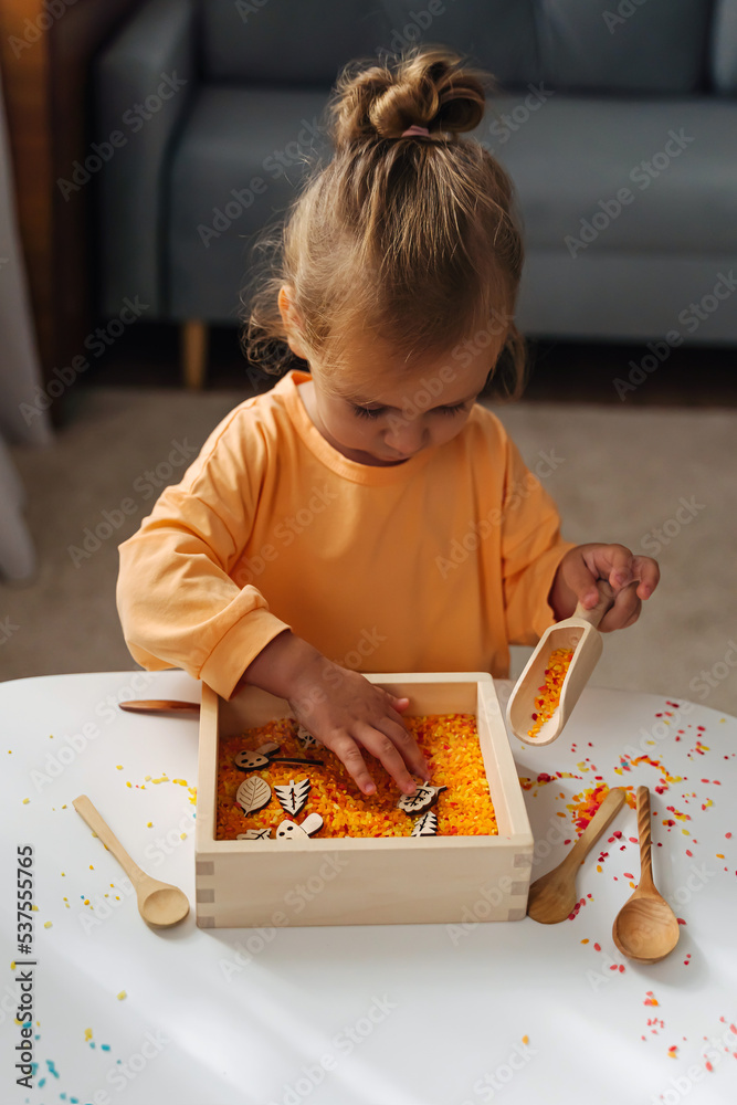 A little girl playing with colored rice in autumn sensory bin ...