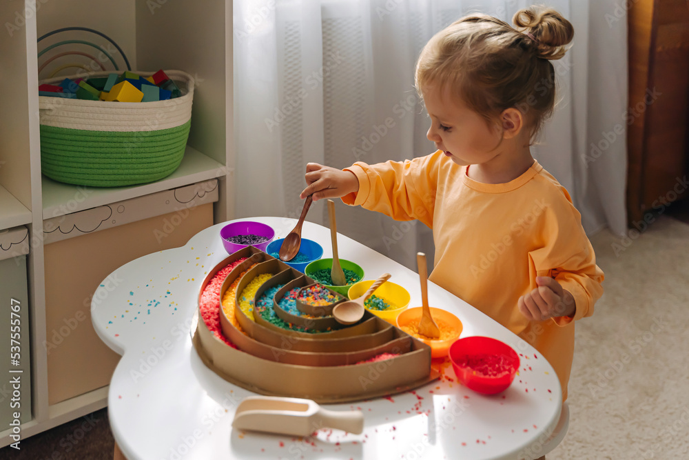 A little girl playing colored rice and make rainbow. Child filled the ...