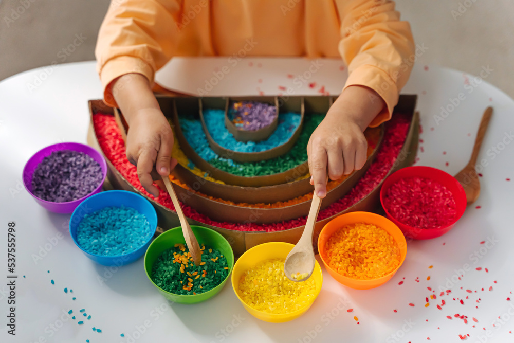 Child hands playing colored rice and make rainbow. Child filled the ...
