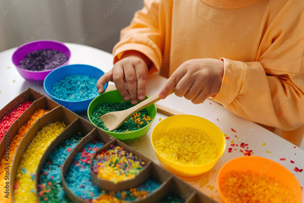 Child hands playing colored rice and make rainbow. Child filled the ...