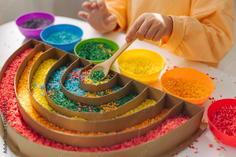 Child hands playing colored rice and make rainbow. Child filled the ...