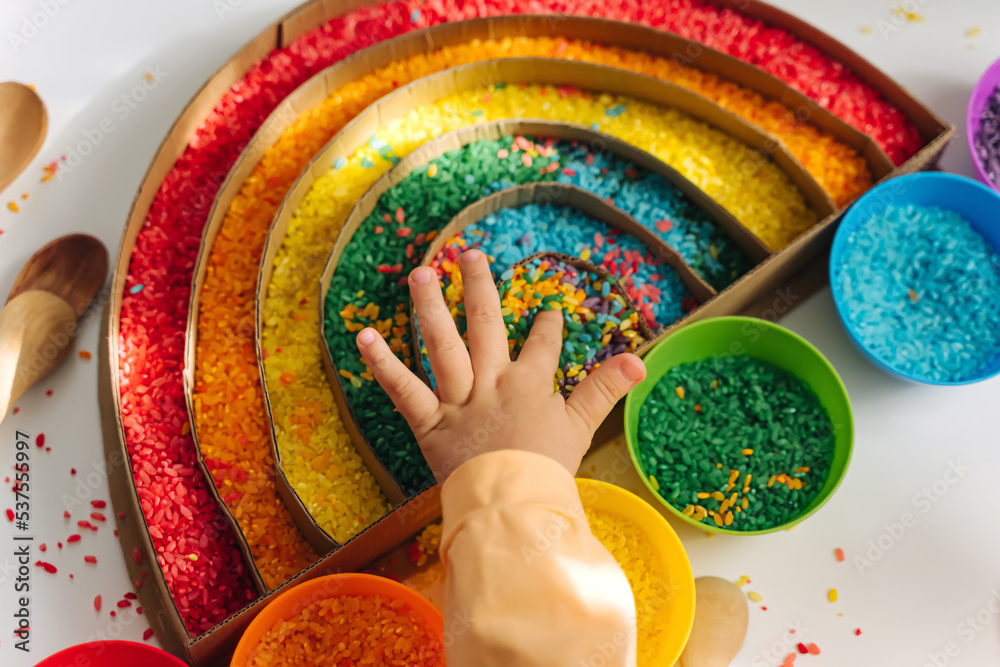 Child hands playing colored rice and make rainbow. Child filled the ...