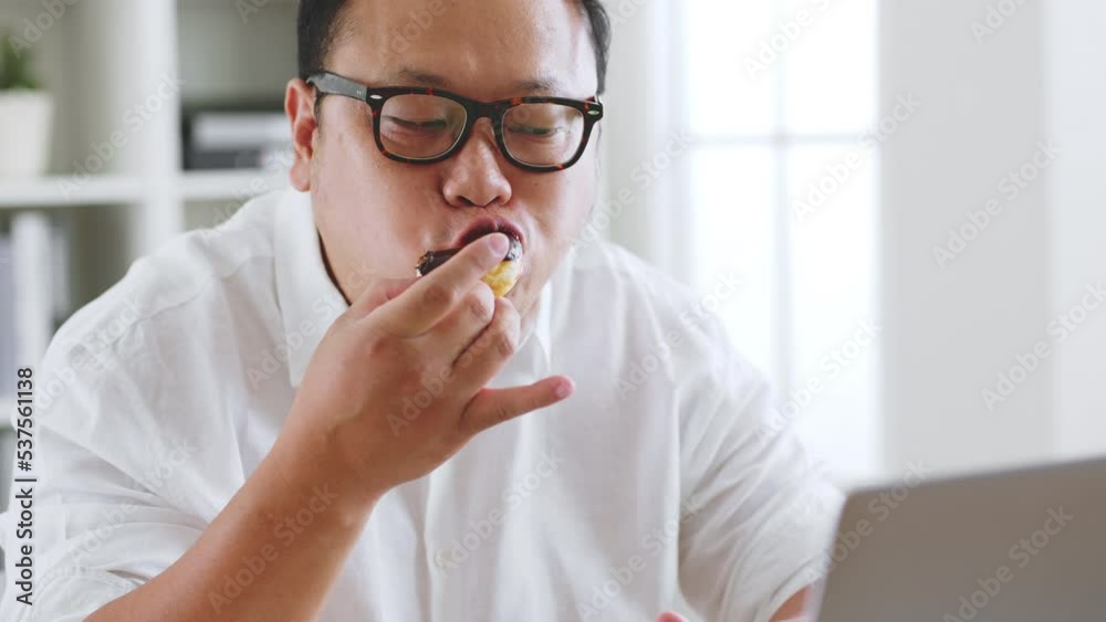 Asian fat man eating donut, sweet, junk food during working with ...