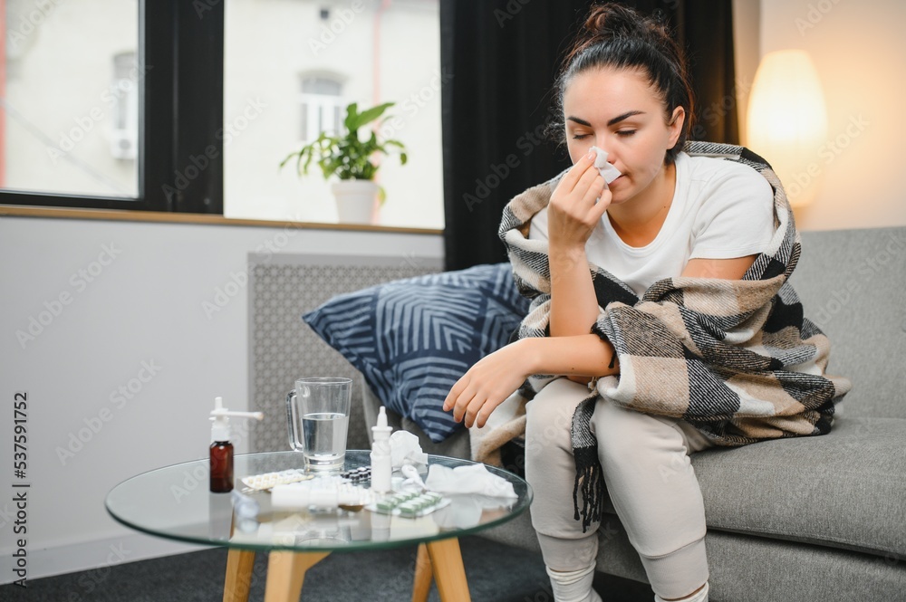 Ill young woman sit on sofa covered with blanket, freezing, blowing her ...