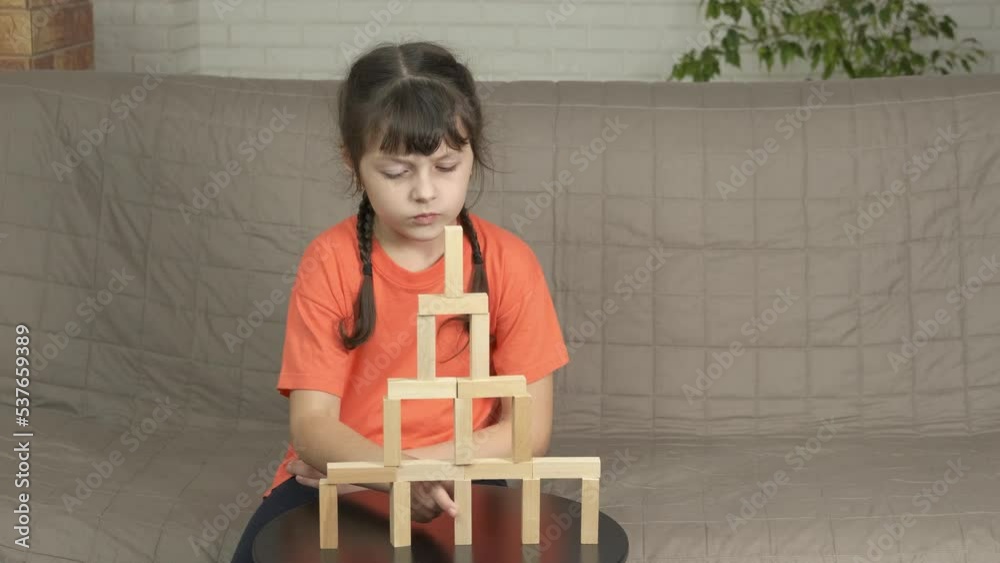 Destroy tower from wooden blocks. A stressed little girl destroy wooden ...