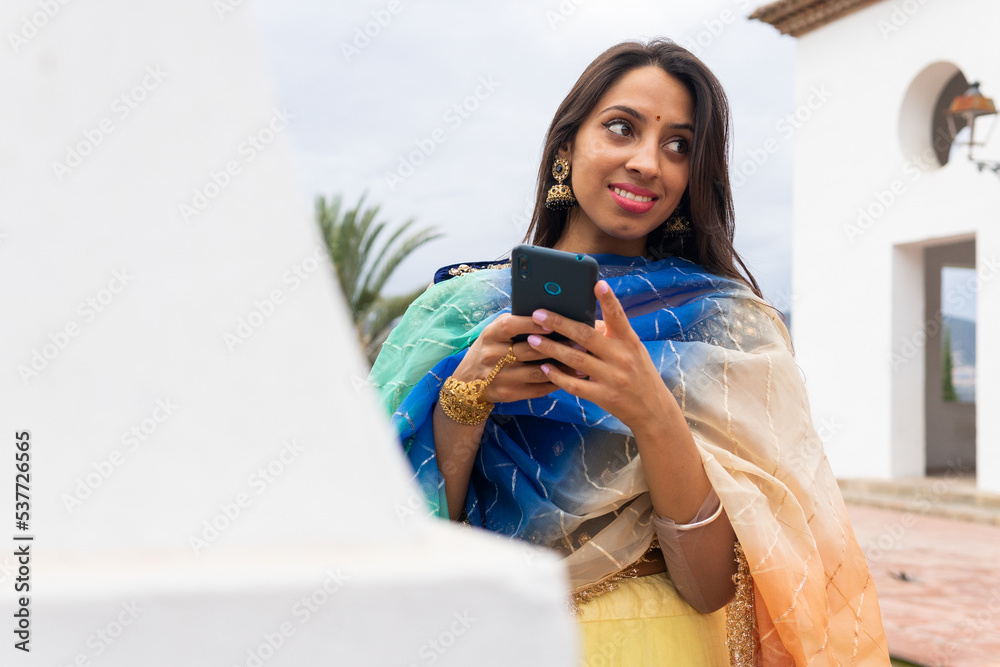 Satisfied Indian woman in traditional outfit texting via mobile phone ...
