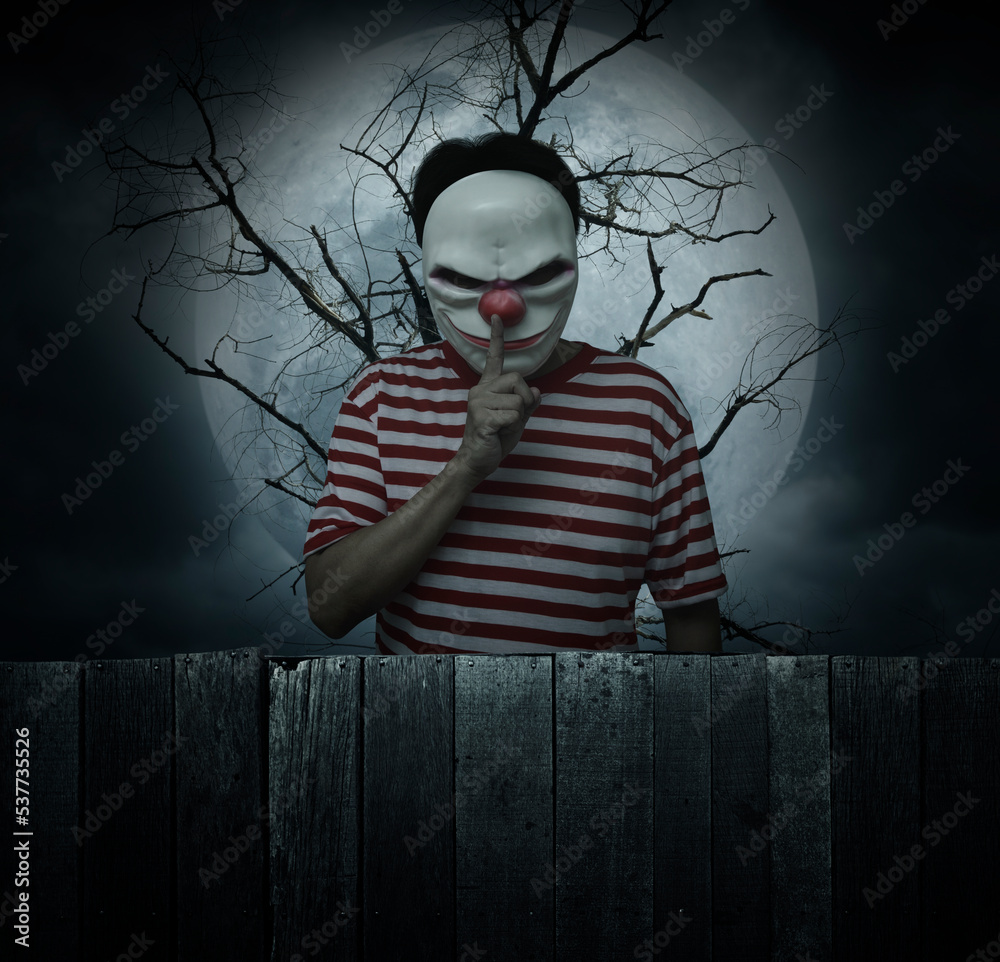 Scary evil clown showing silence sign with finger over lips standing ...