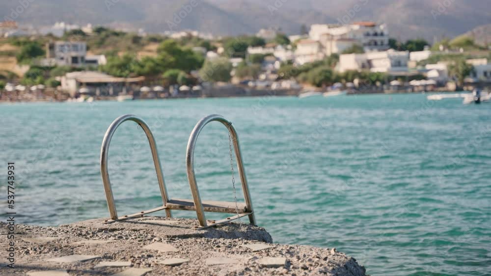 Metal ladder with beach and tavernas in background on greek island in ...