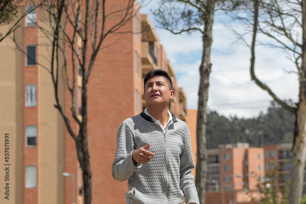 A young Latino man throwing a small object into the air on a sunny day ...