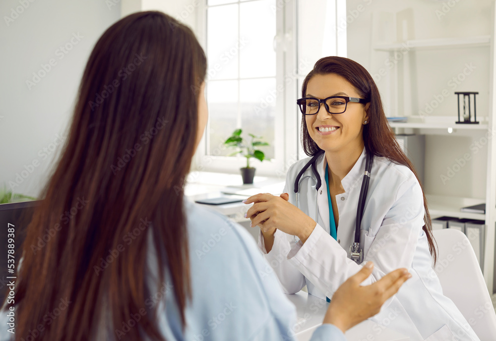 Young woman talking to doctor at modern clinic. Happy female physician ...