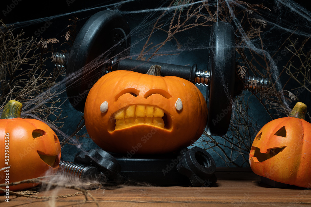 Carved Halloween pumpkin lifting a heavy barbell dumbbell ...