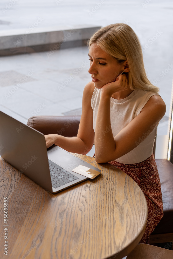 Blonde woman using a laptop with a credit card in a coffee shop ...