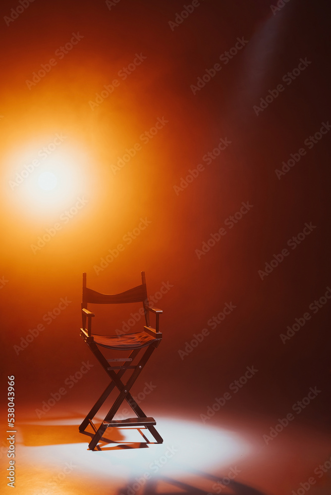 The director's chair stands in a beam of light with an orange backlight ...