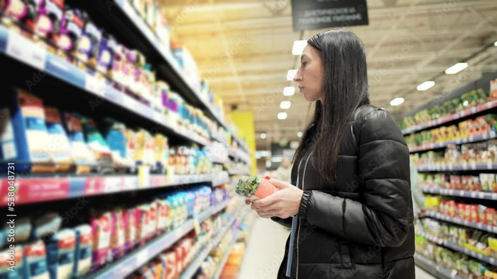 Shopping of food. A young woman chooses products in supermarket. Woman ...
