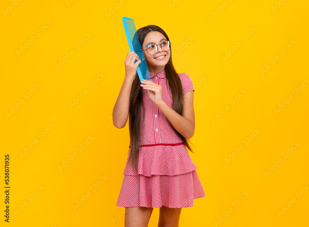 Teenager brushing combing hair with big comb on yellow isolated studio ...