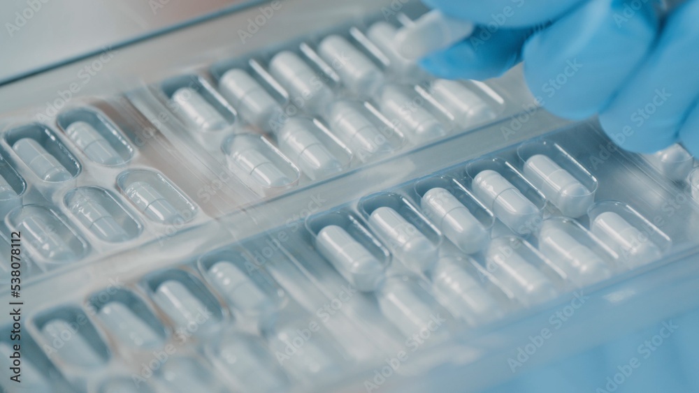 Pharmacologist checks blister packs with medicinal capsules moving on a ...