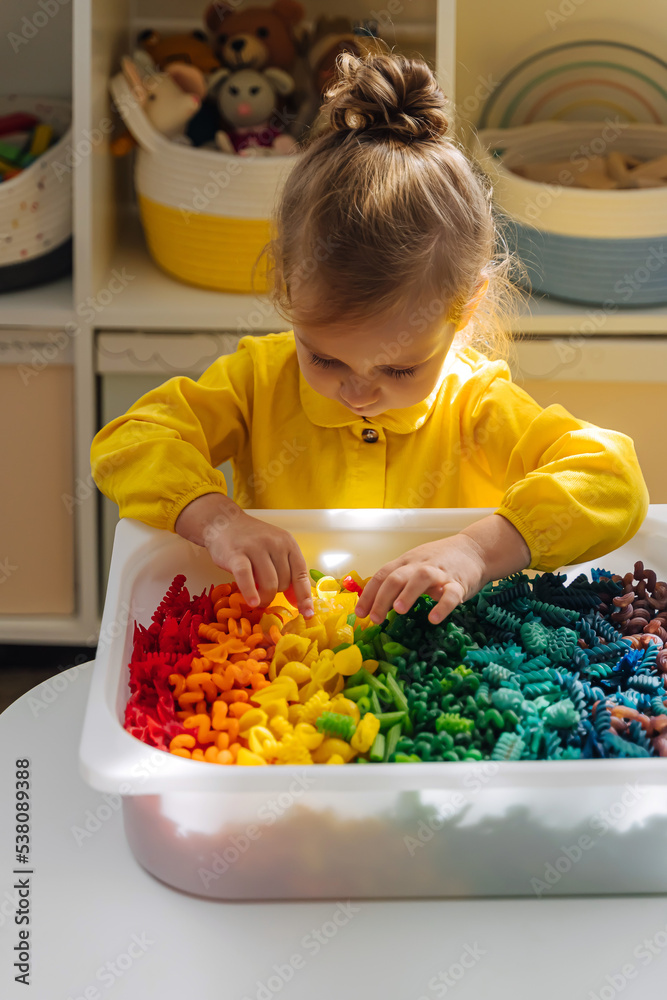 Foto de Child playing with sensory bin with dried pasta in rainbow ...