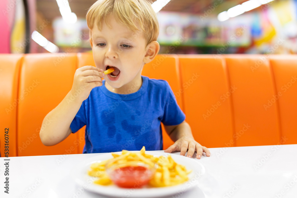 Cute child eating french fries with sauce at table in fast food ...