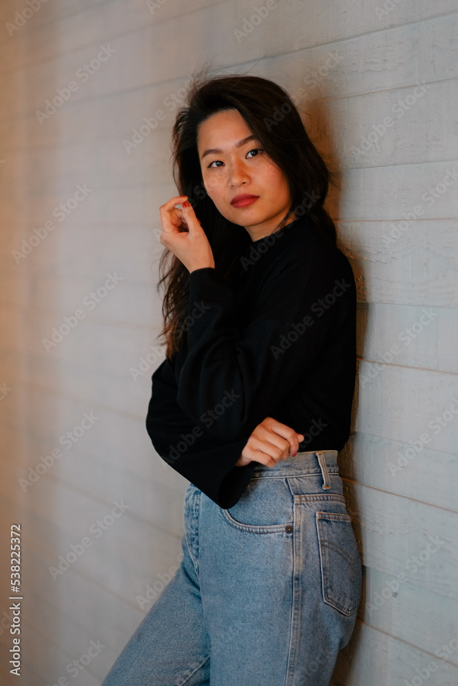 Southeast Asian woman wearing dark sweater and light jeans, leans on a ...