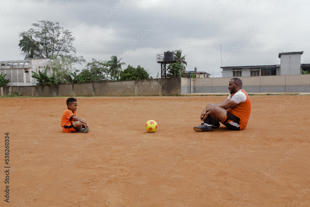 Foto de Father and son sitting on soccer field with their legs crossed ...