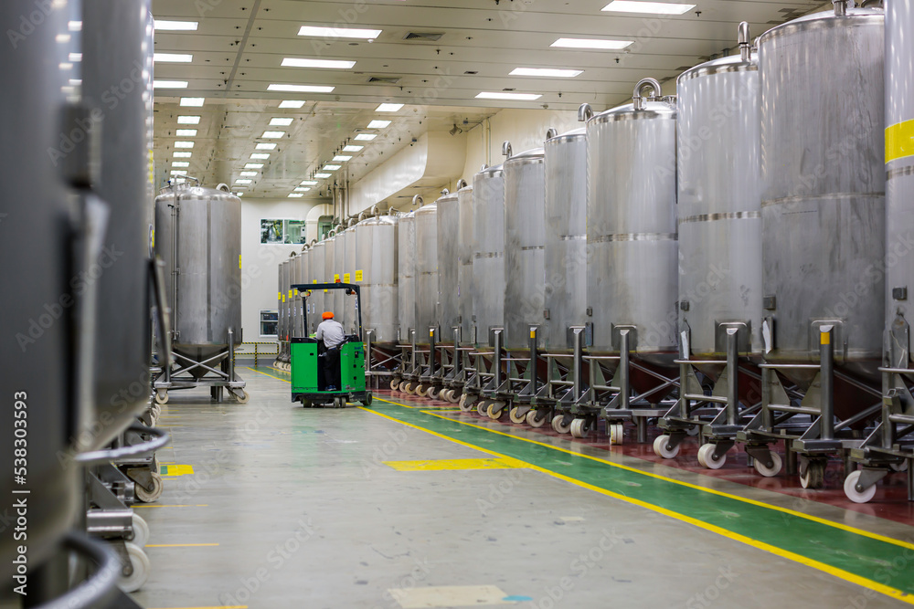 A male worker moving a bucket stainless vertical steel tanks equipment ...