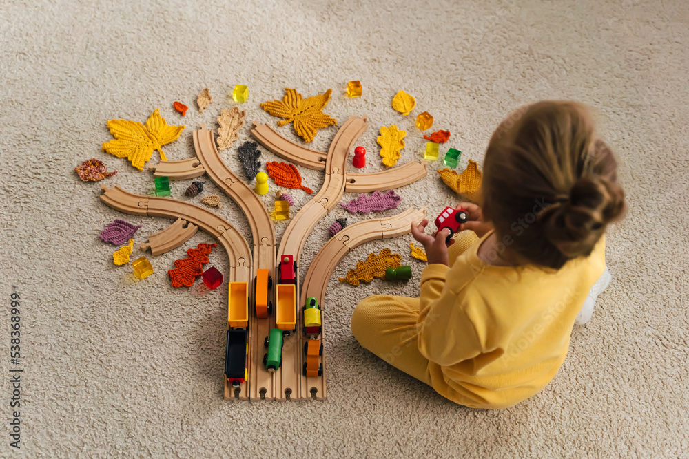 A little girl playing with autumn leaves and make a tree with wooden ...