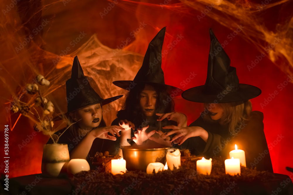 Three young girls dressed in witch's attire are conjuring over the ...